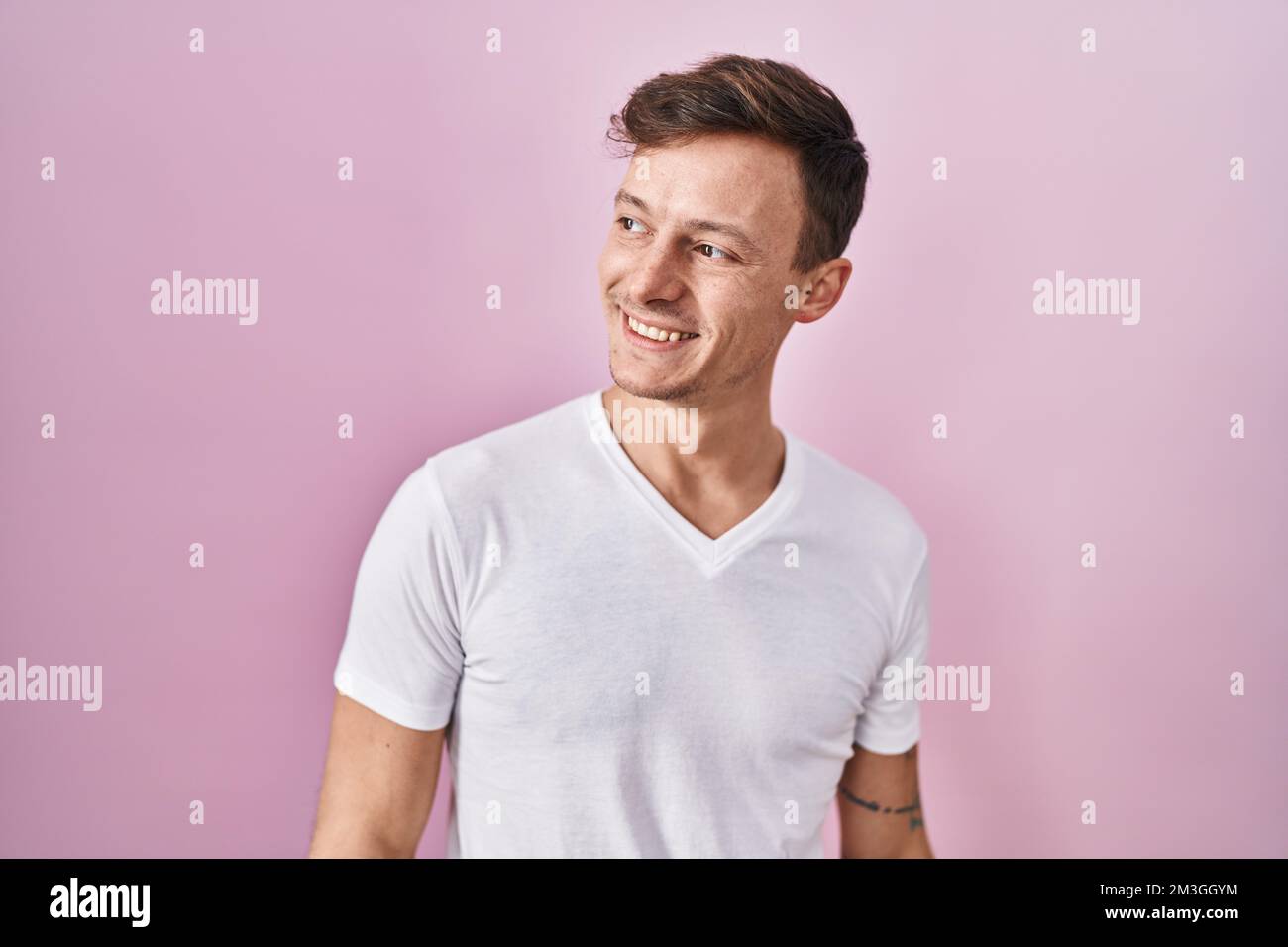 Caucasian man standing over pink background looking away to side with ...