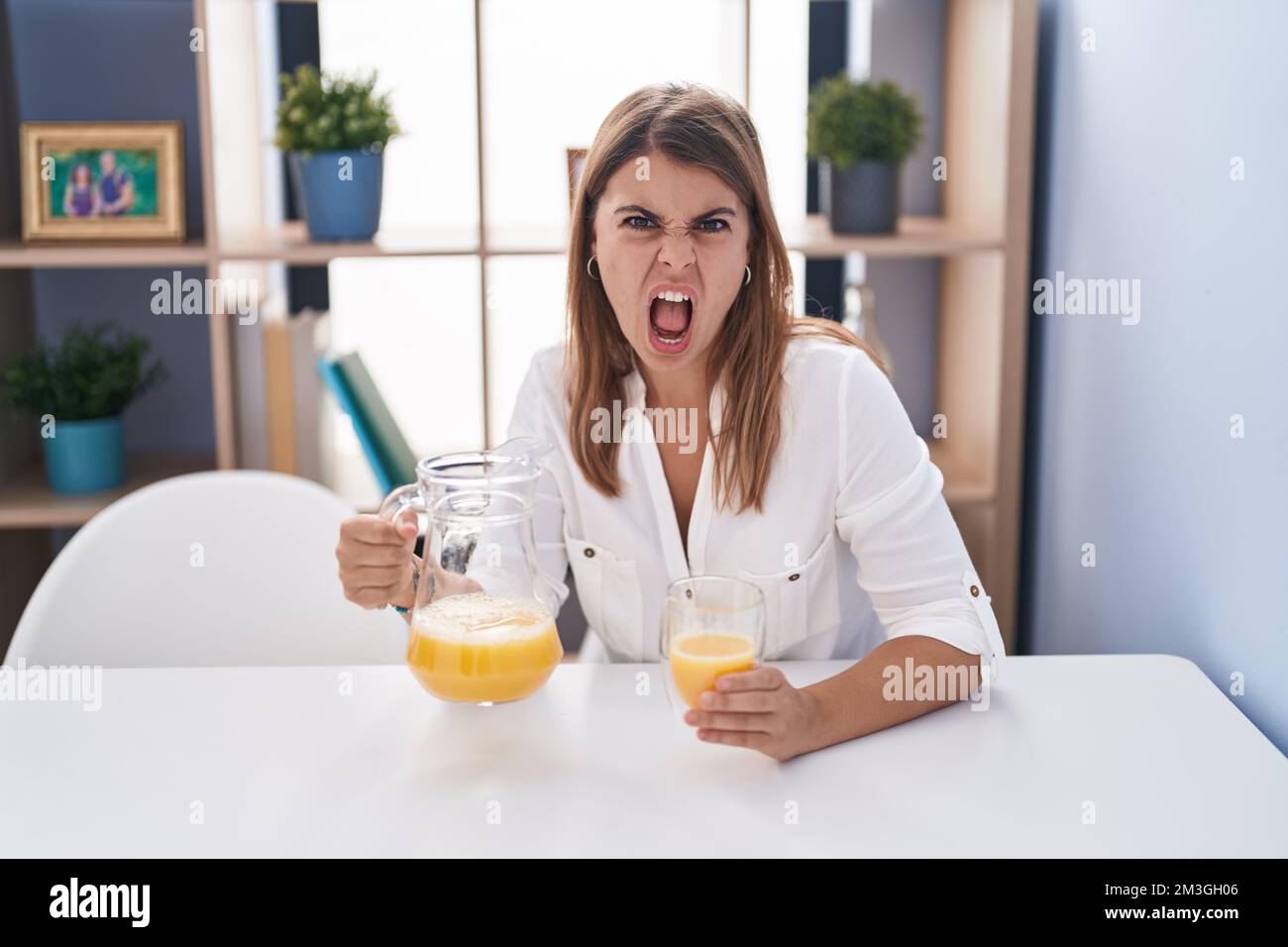 Young hispanic woman drinking glass of orange juice angry and mad ...