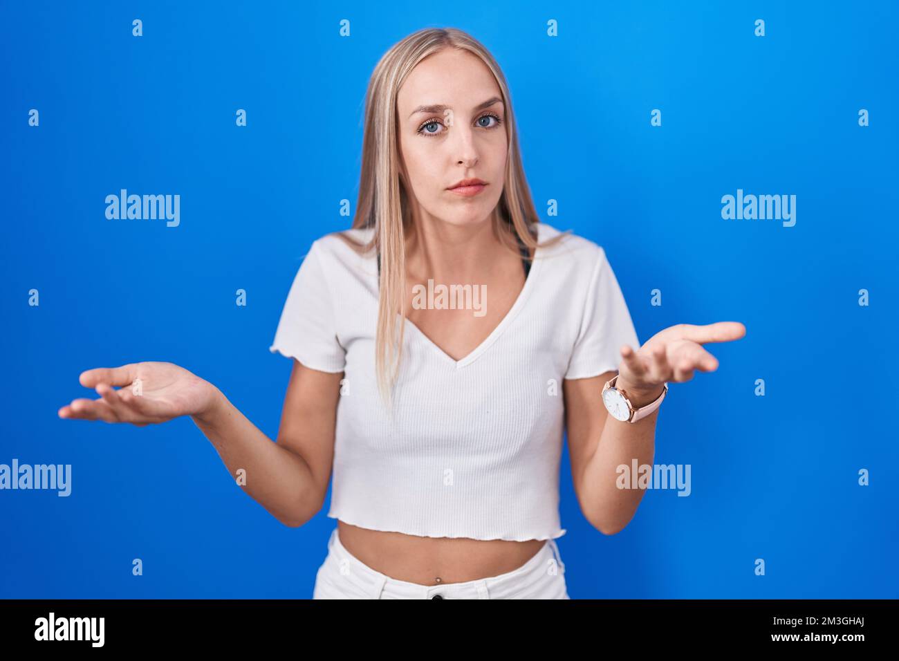 Young caucasian woman standing over blue background clueless and ...