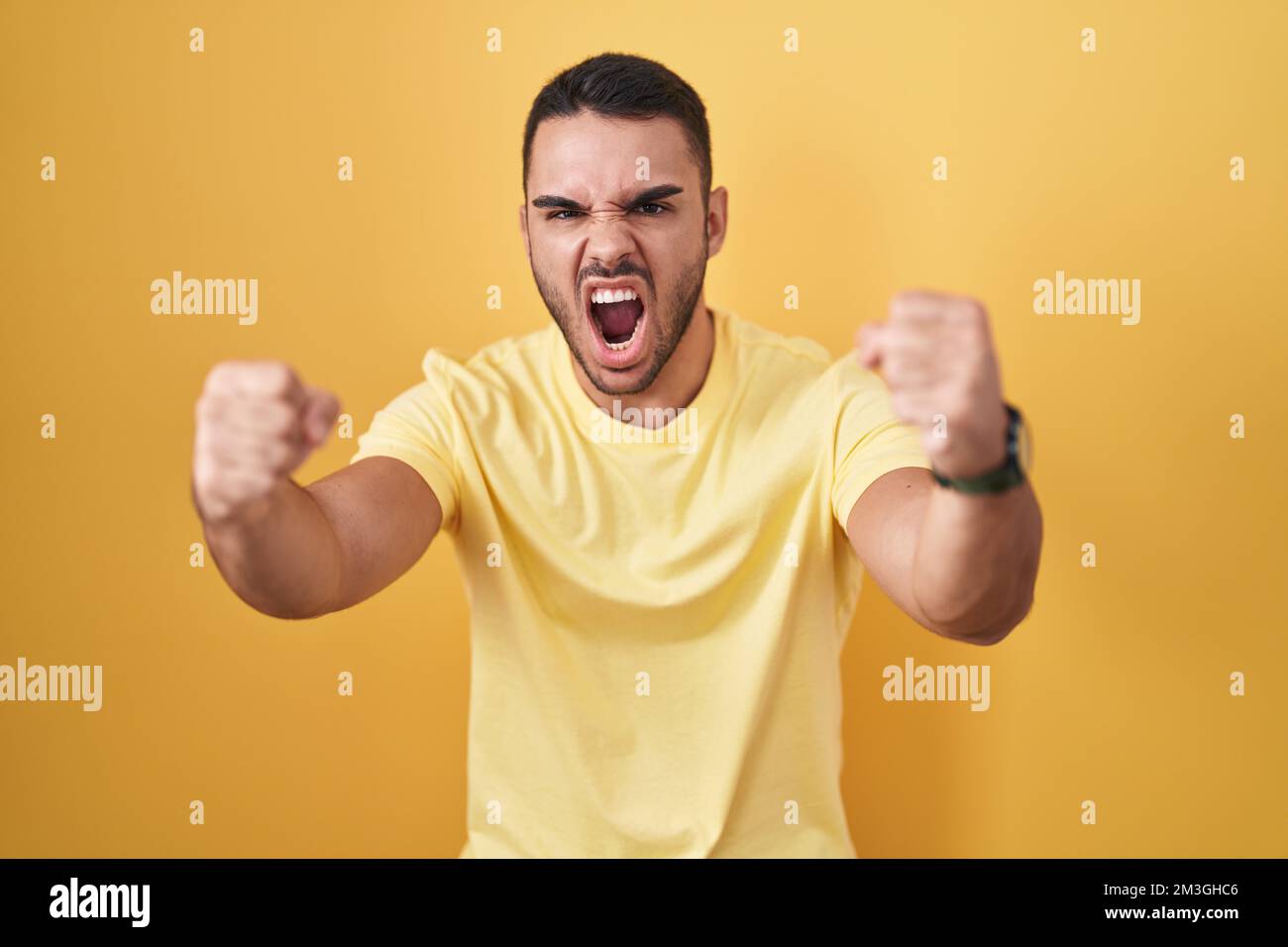 Young hispanic man standing over yellow background angry and mad ...