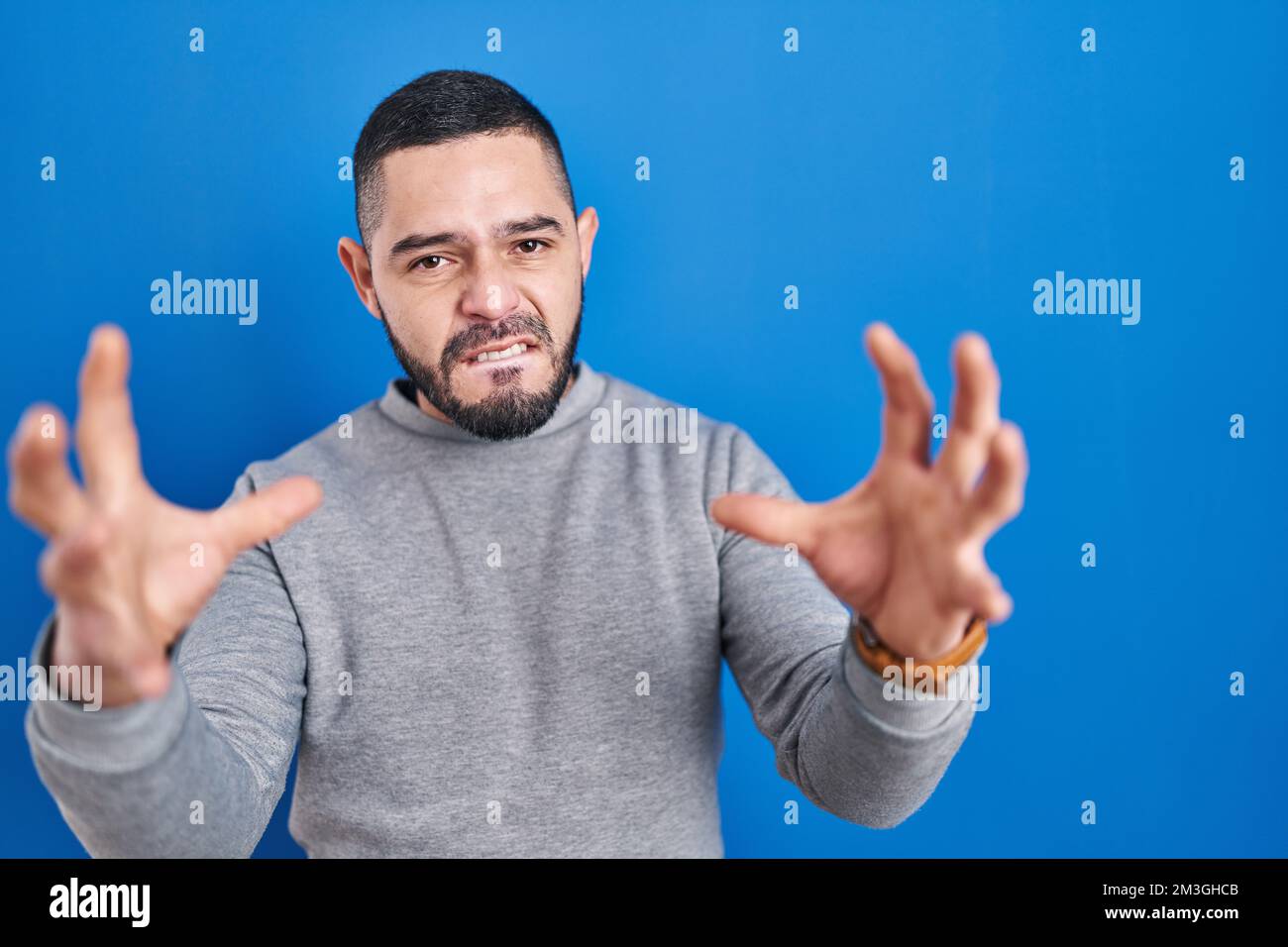 Hispanic man standing over blue background shouting frustrated with ...