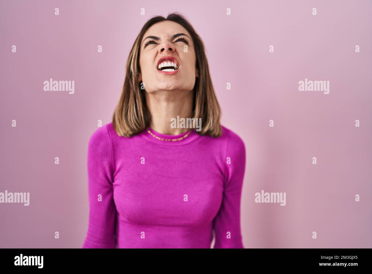 Hispanic woman standing over pink background angry and mad screaming ...