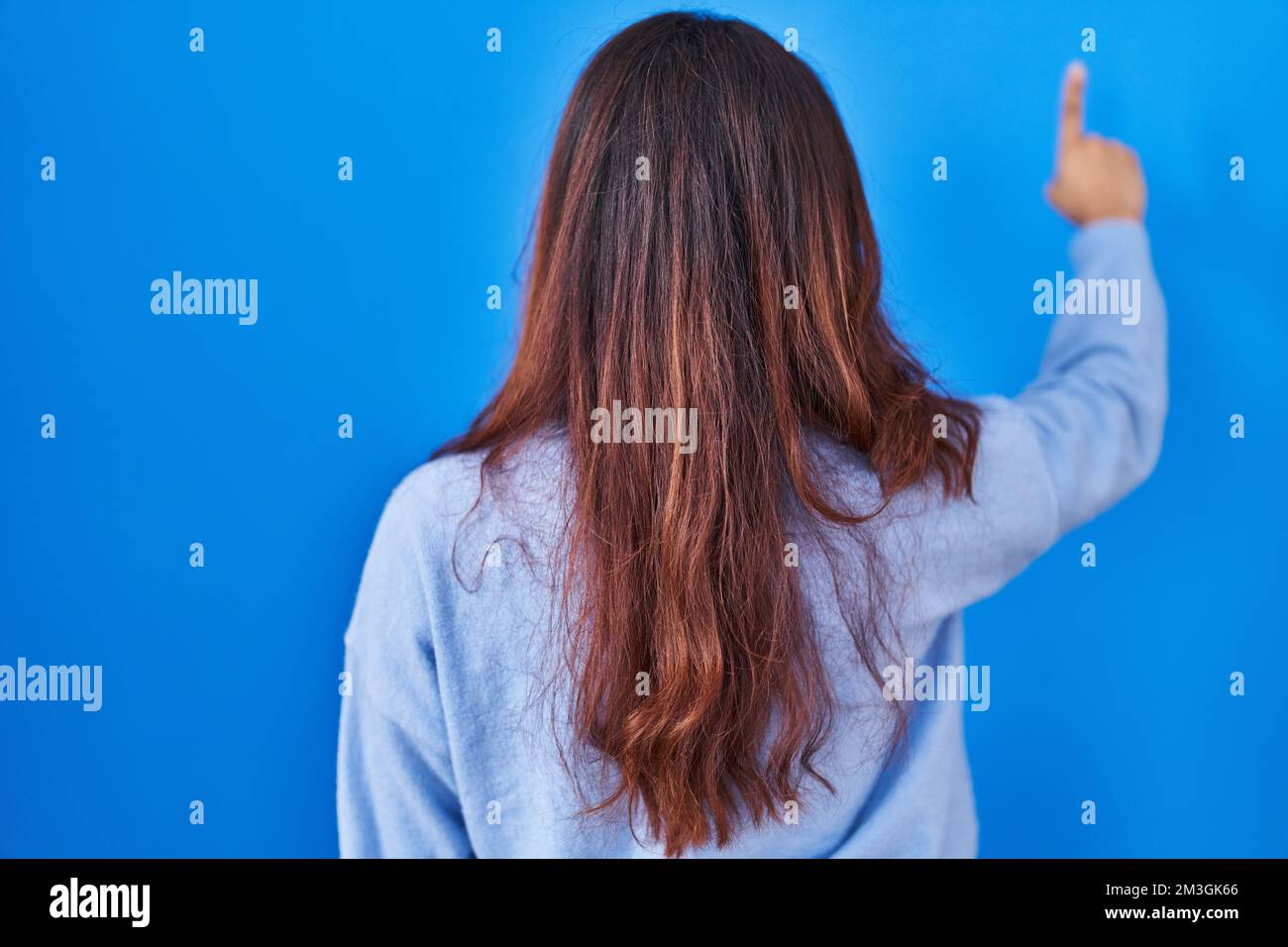 Hispanic young woman standing over blue background posing backwards ...