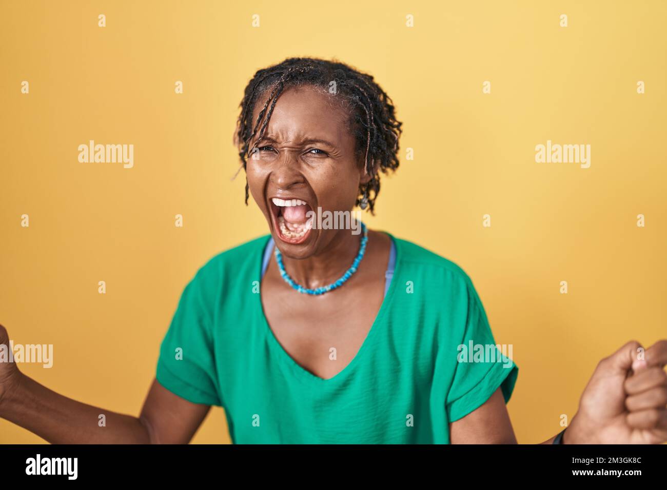 African woman with dreadlocks standing over yellow background angry and ...