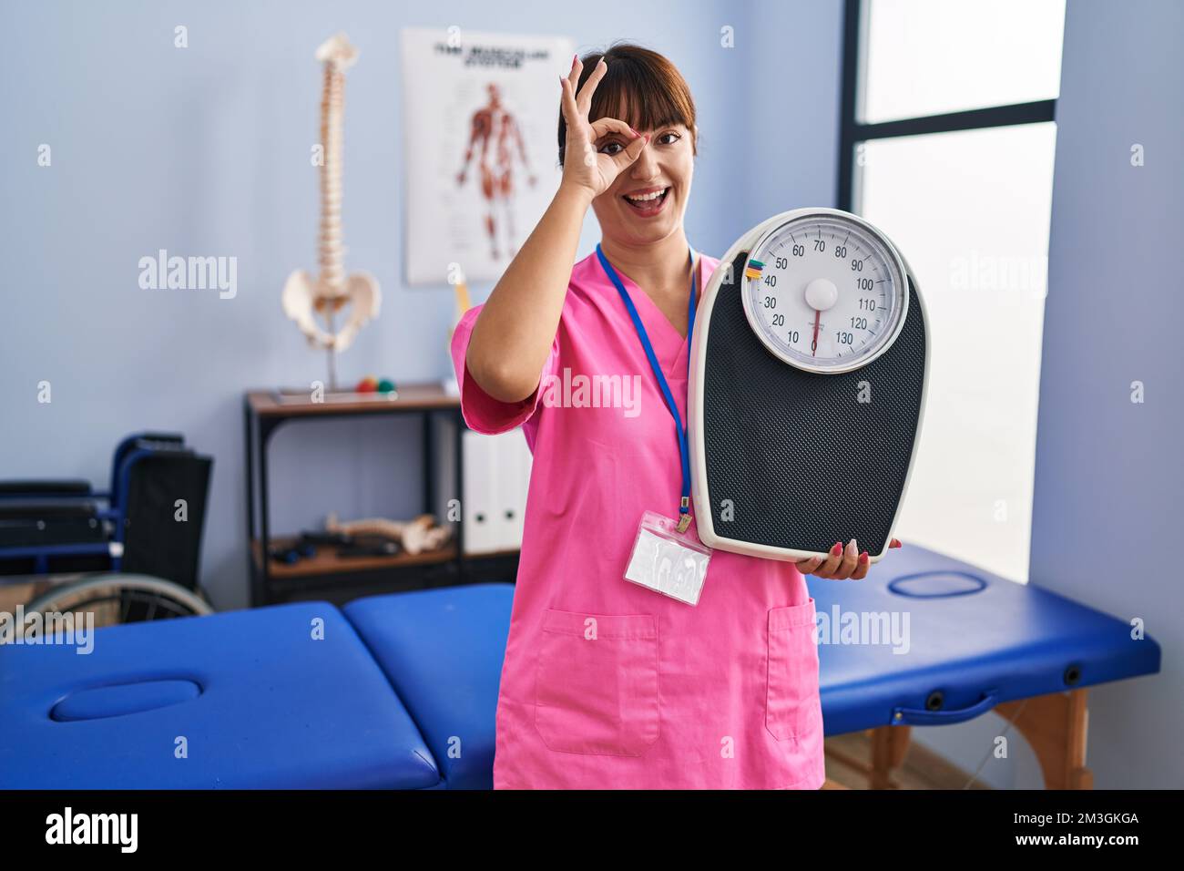 Young brunette woman as nutritionist holding weighing machine smiling ...