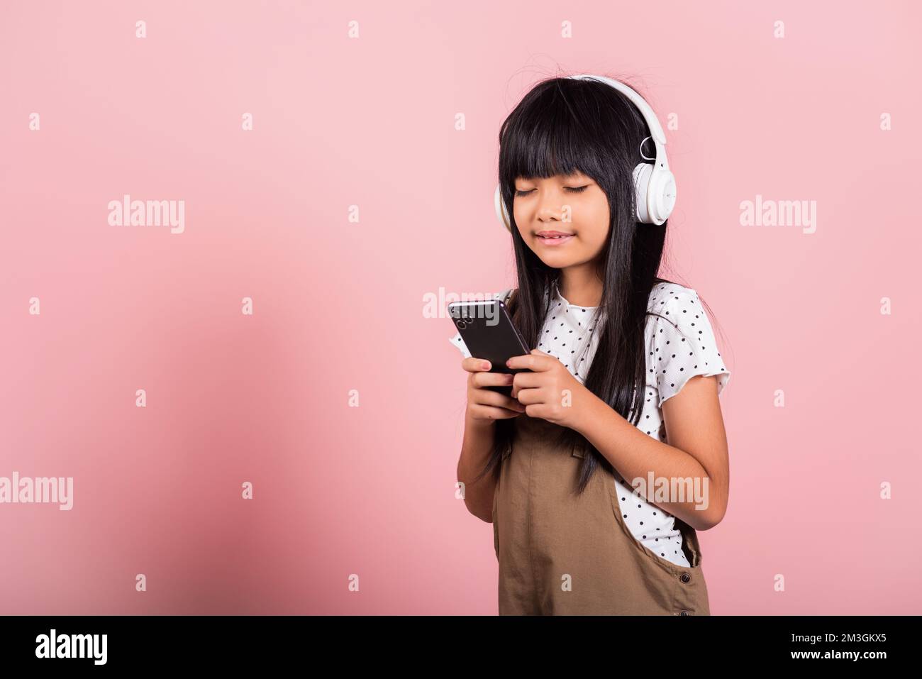 Asian kid 10 years enjoying listening music from mobile phone wear ...