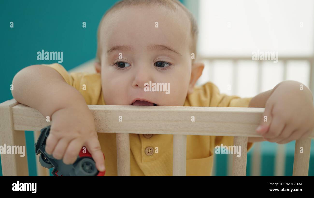 Adorable hispanic baby standing on cradle sucking wooden balustrade at ...