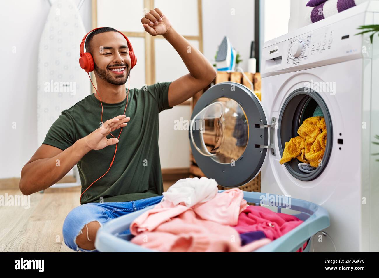 Young hispanic man listening to music using washing machine at laundry ...