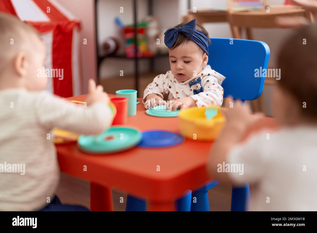 Group of toddlers learning to eat sitting on table at kindergarten ...