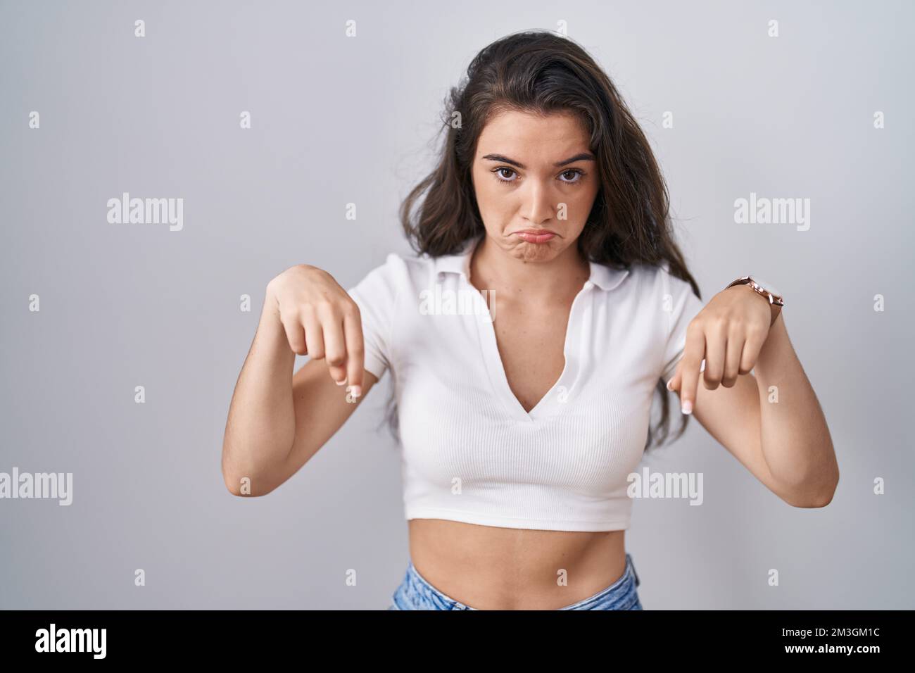 Young teenager girl standing over white background pointing down ...