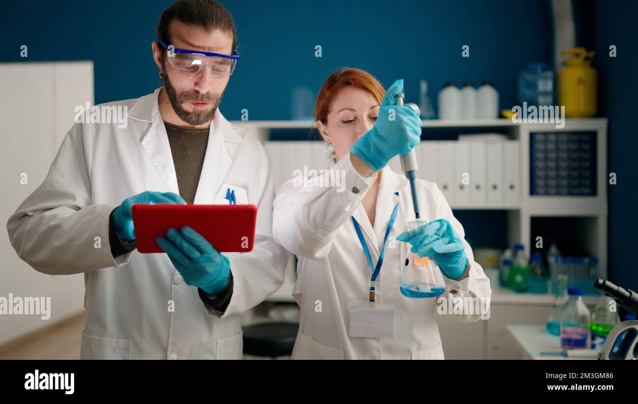 Man and woman wearing sciencist uniform using touchpad at laboratory ...