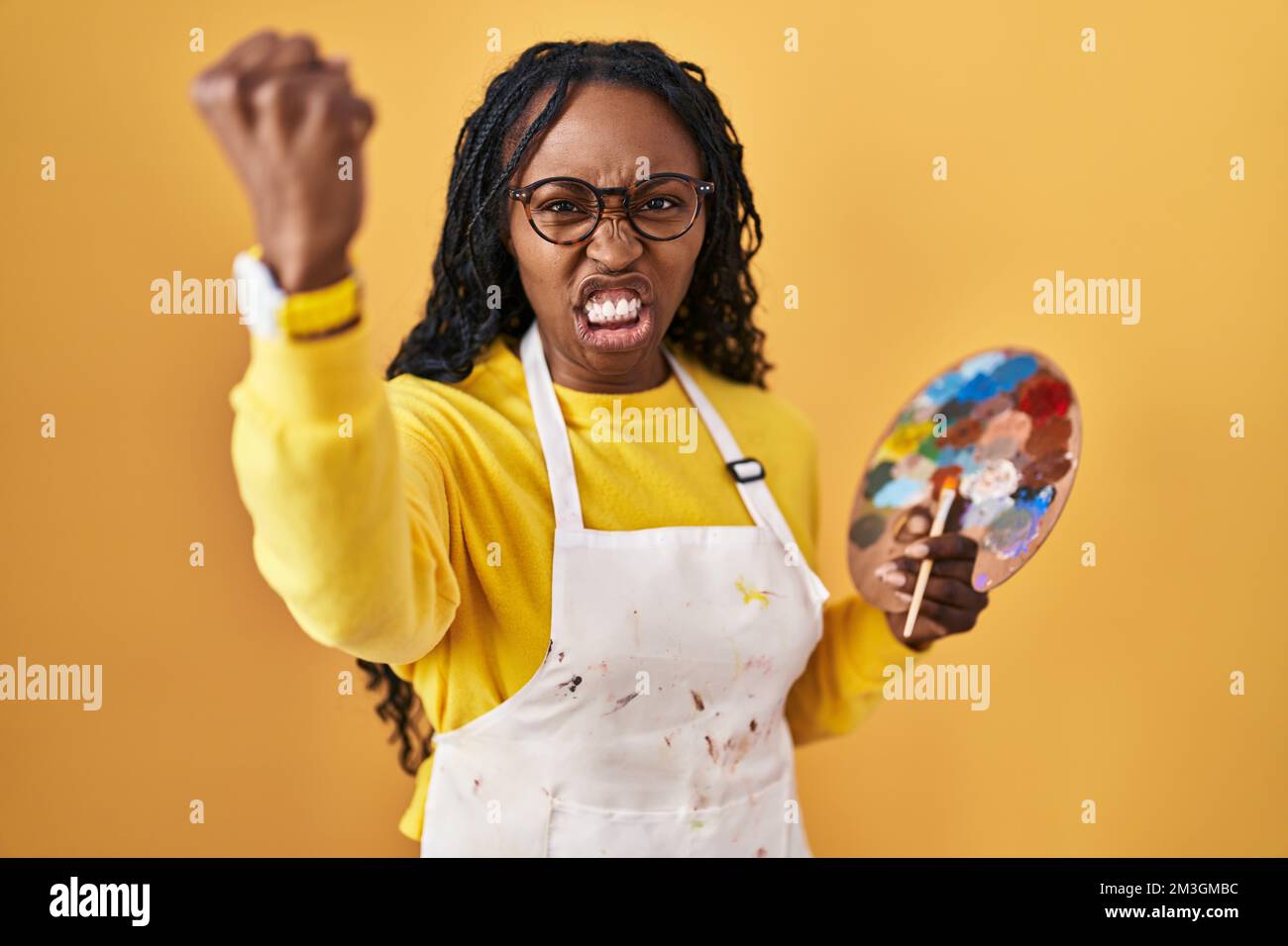 African woman holding painter palette angry and mad raising fist ...