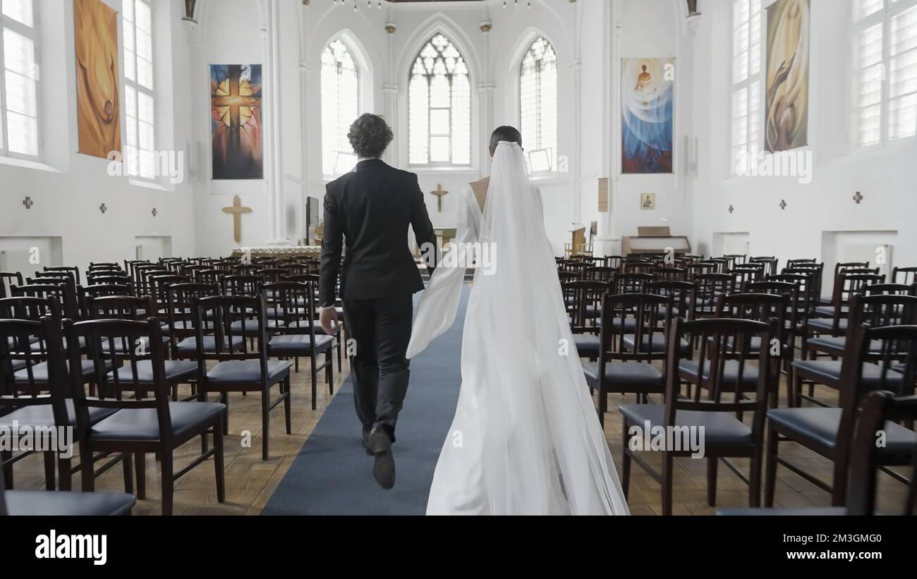 Beautiful newlyweds walking down aisle. Action. Rear view of couple of ...