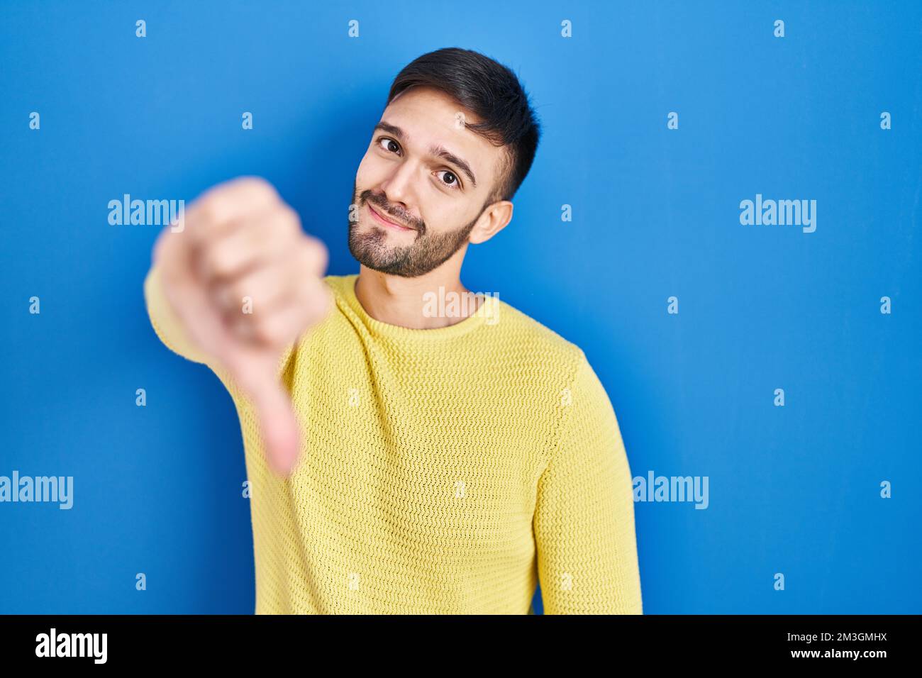 Hispanic man standing over blue background looking unhappy and angry ...