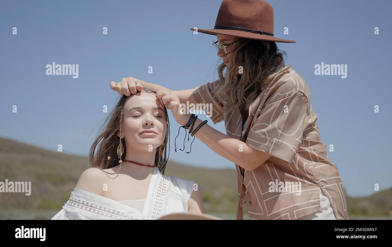 Female stylist preparing a young model for the photosession outdoors on ...
