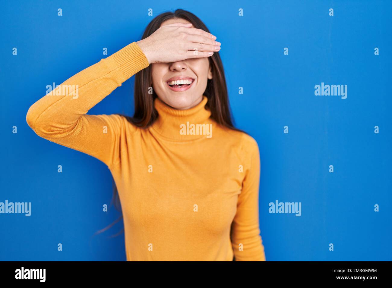Young brunette woman standing over blue background smiling and laughing ...