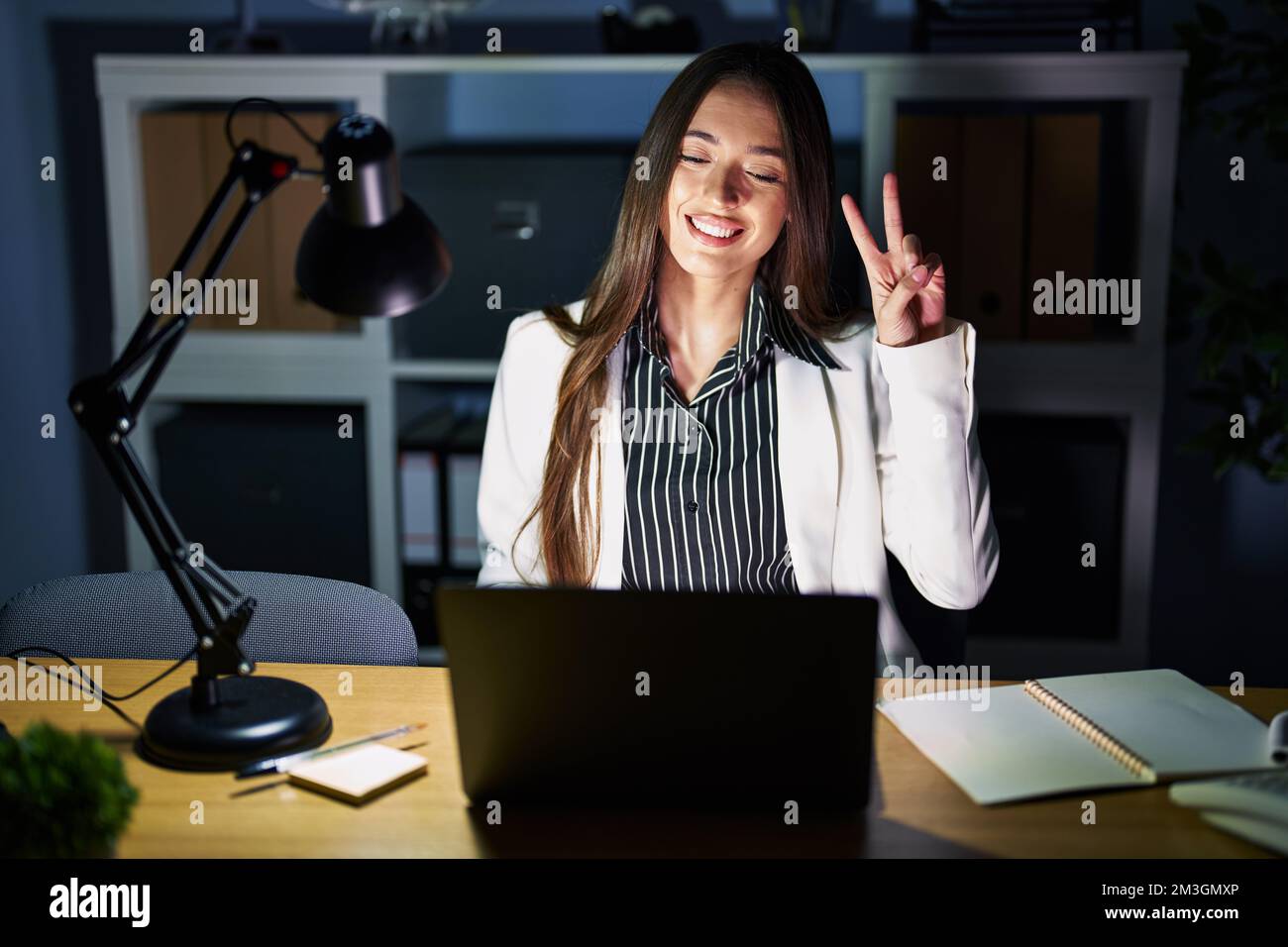 Young brunette woman working at the office at night with laptop smiling ...
