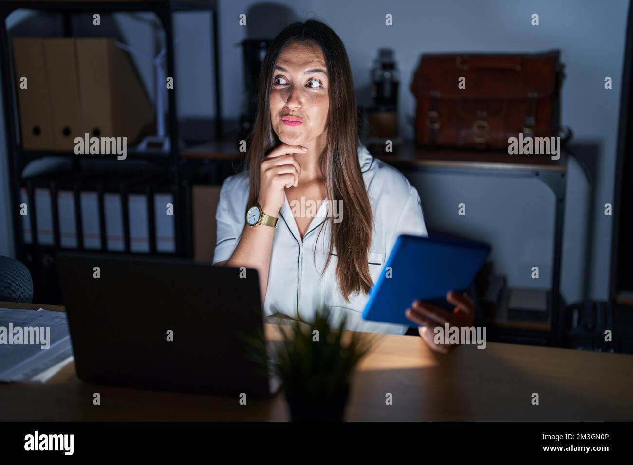 Young brunette woman working at the office at night smiling looking to ...