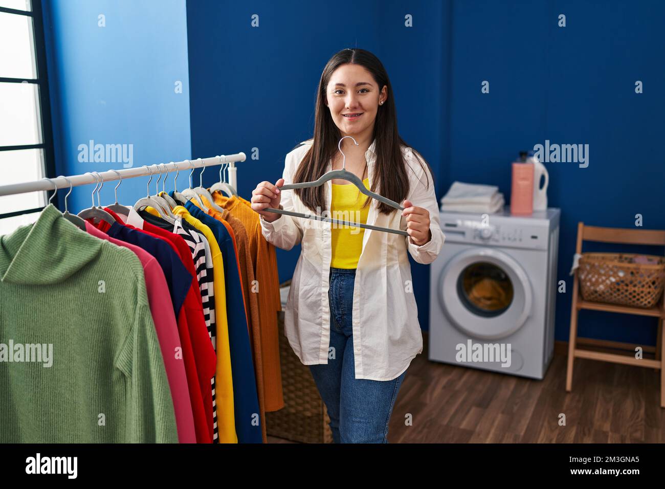 Young latin woman putting clean laundry on hangers smiling with a happy ...
