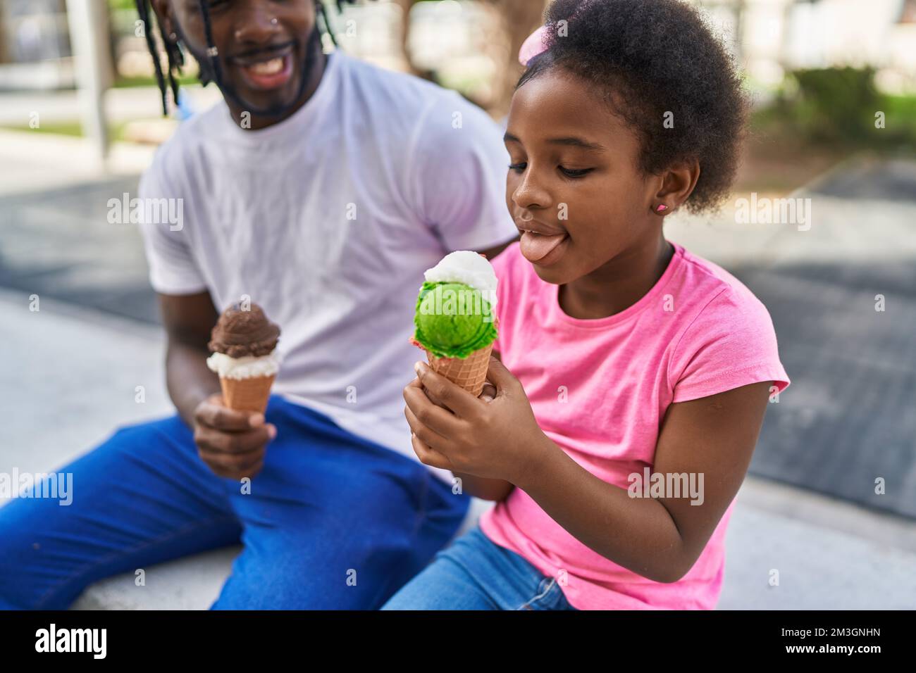 Father and daughter eating ice cream sitting together on bench at park ...