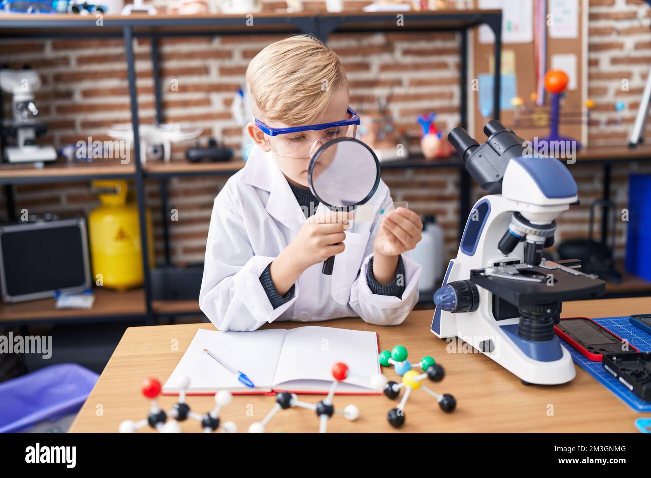 Adorable toddler student looking sample with magnifying glass at ...
