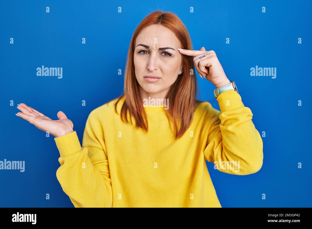 Young woman standing over blue background confused and annoyed with ...