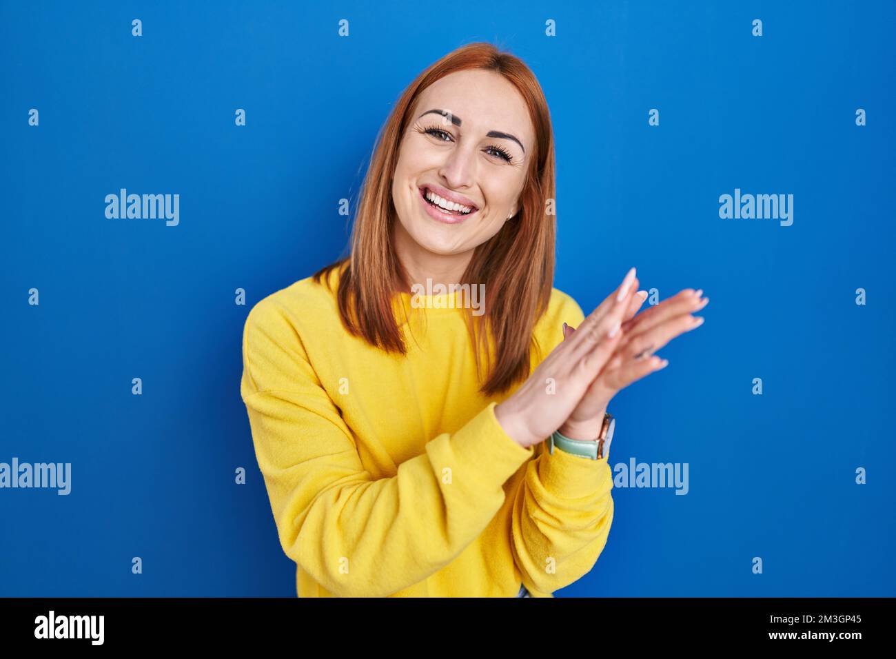 Young woman standing over blue background clapping and applauding happy ...