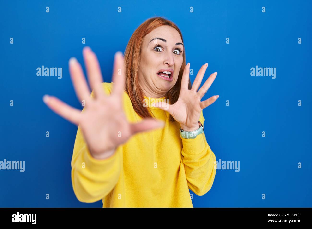Young woman standing over blue background afraid and terrified with ...