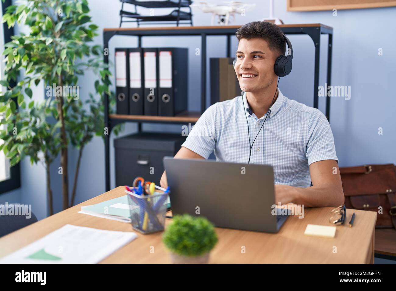 Young hispanic man working at the office wearing headphones smiling ...