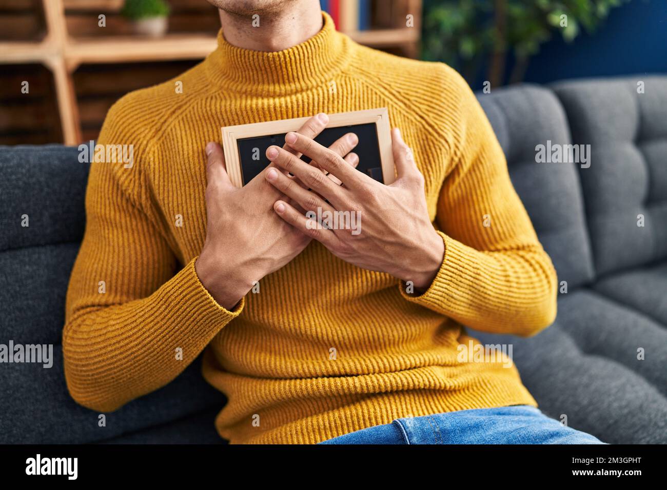Young hispanic man hugging photo frame sitting on sofa at home Stock ...
