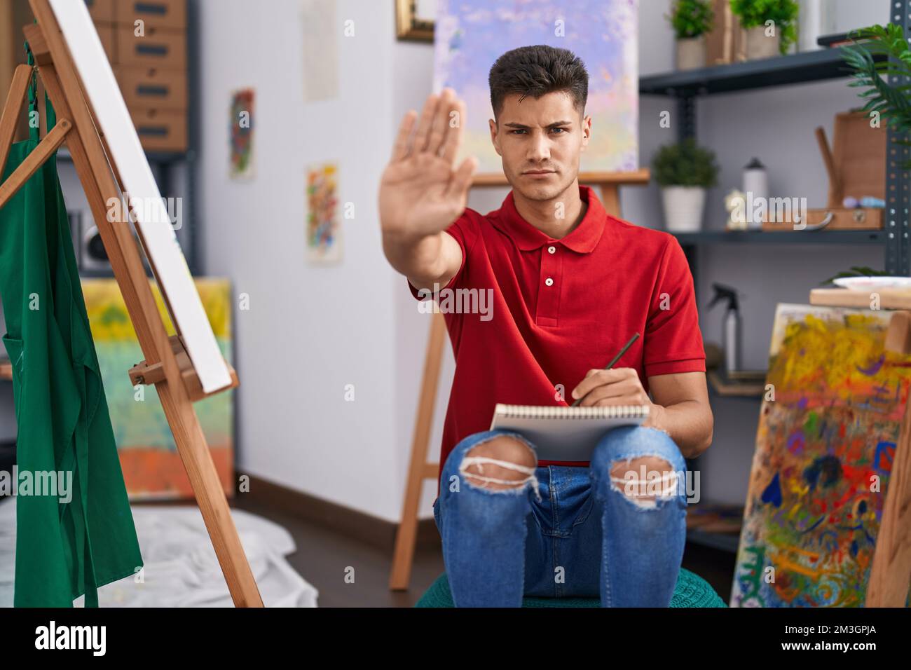 Young hispanic man drawing on art notebook with open hand doing stop ...