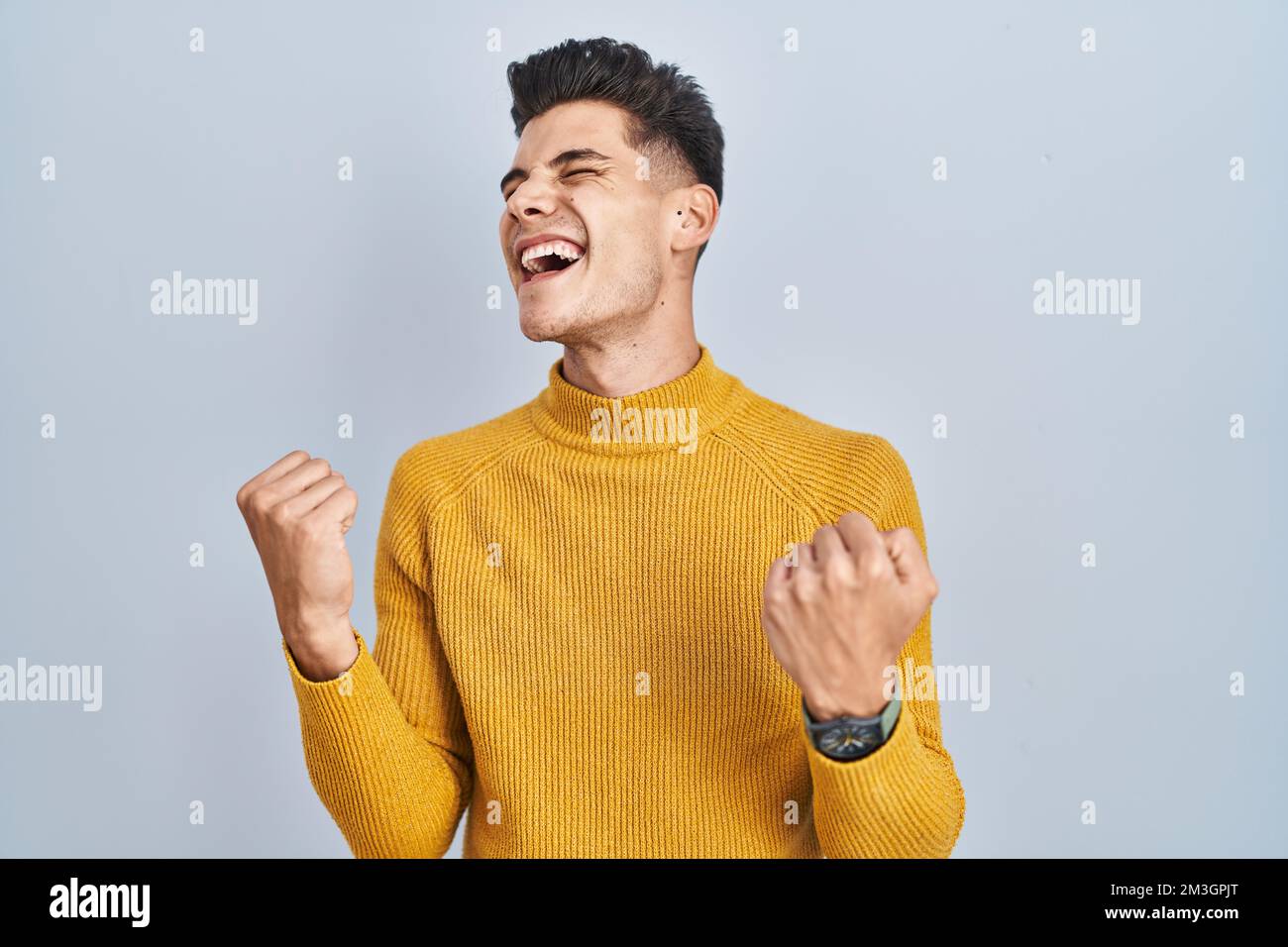 Young hispanic man standing over blue background celebrating surprised ...