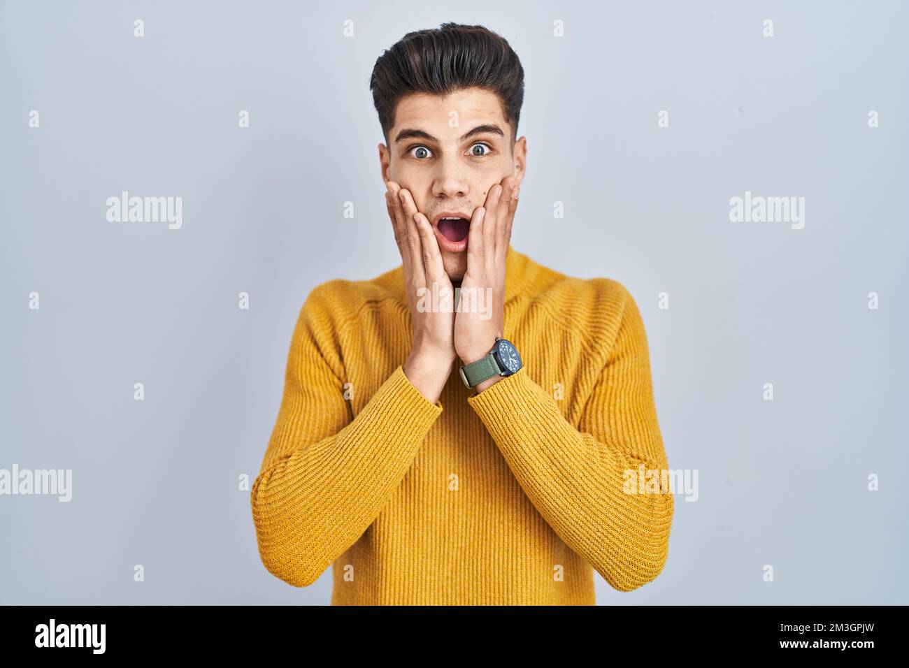 Young hispanic man standing over blue background afraid and shocked ...