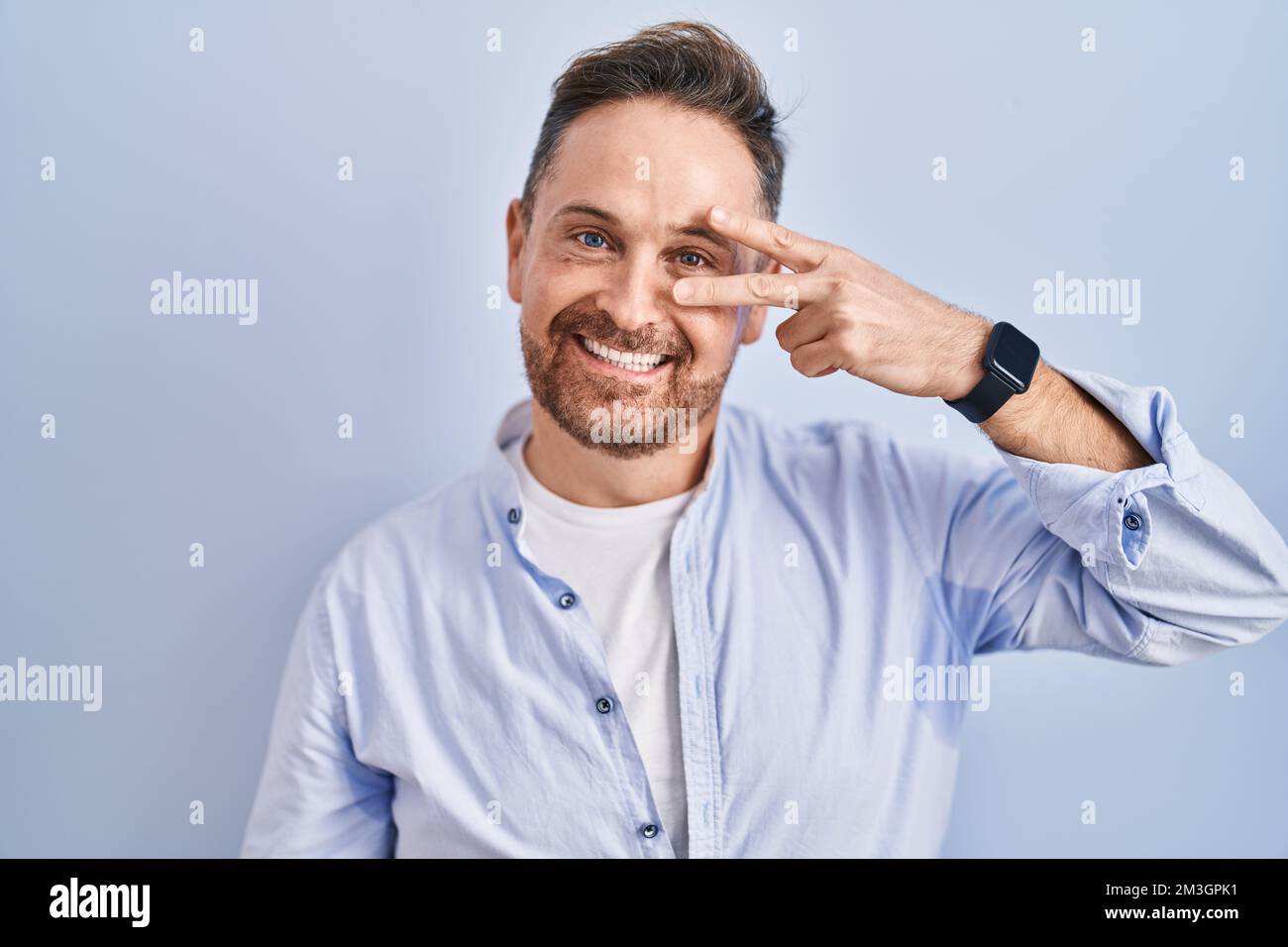 Middle age caucasian man standing over blue background doing peace ...