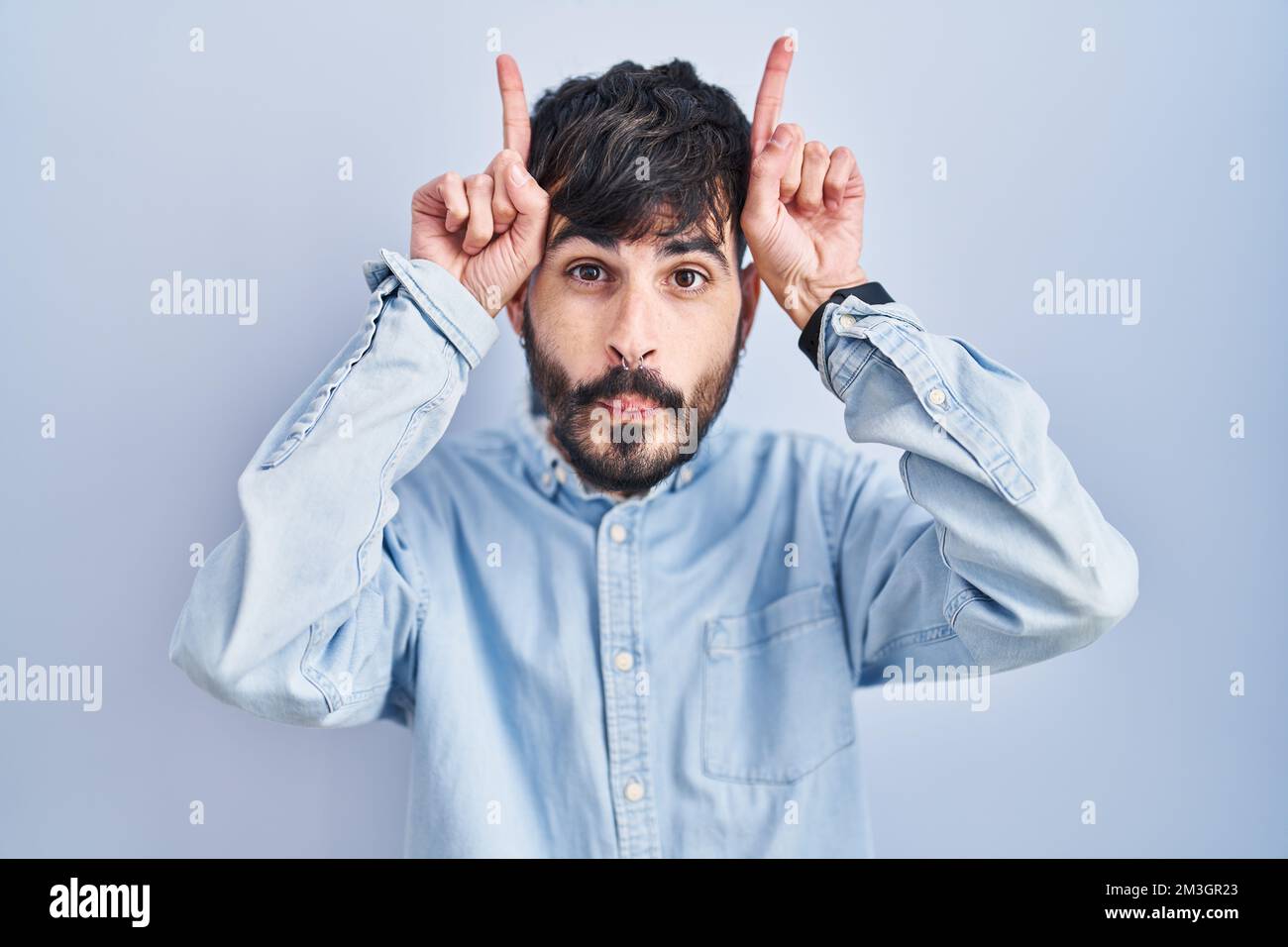 Young hispanic man with beard standing over blue background doing funny ...