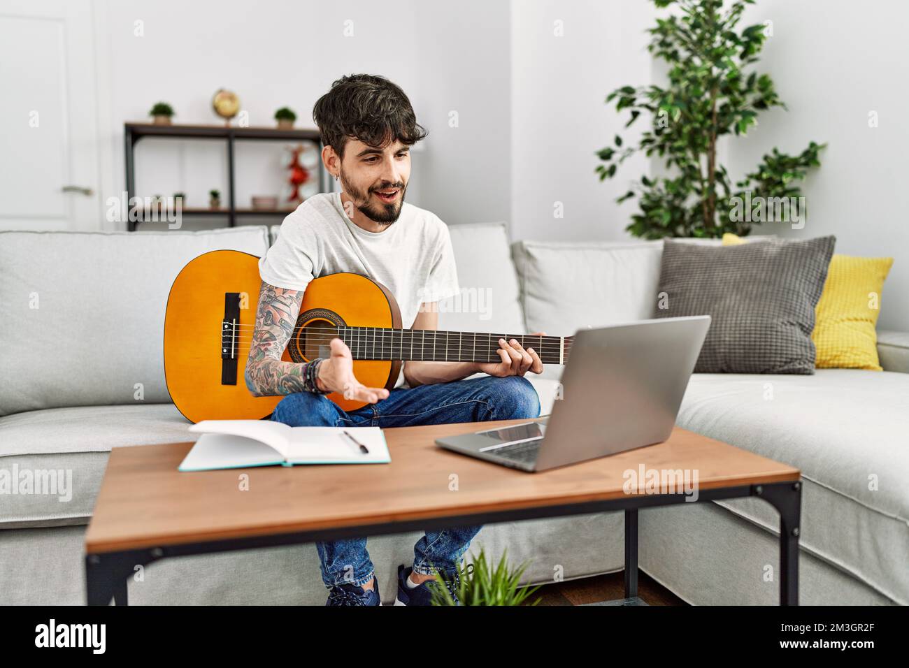 Young hispanic man playing classical guitar and using laptop at home ...