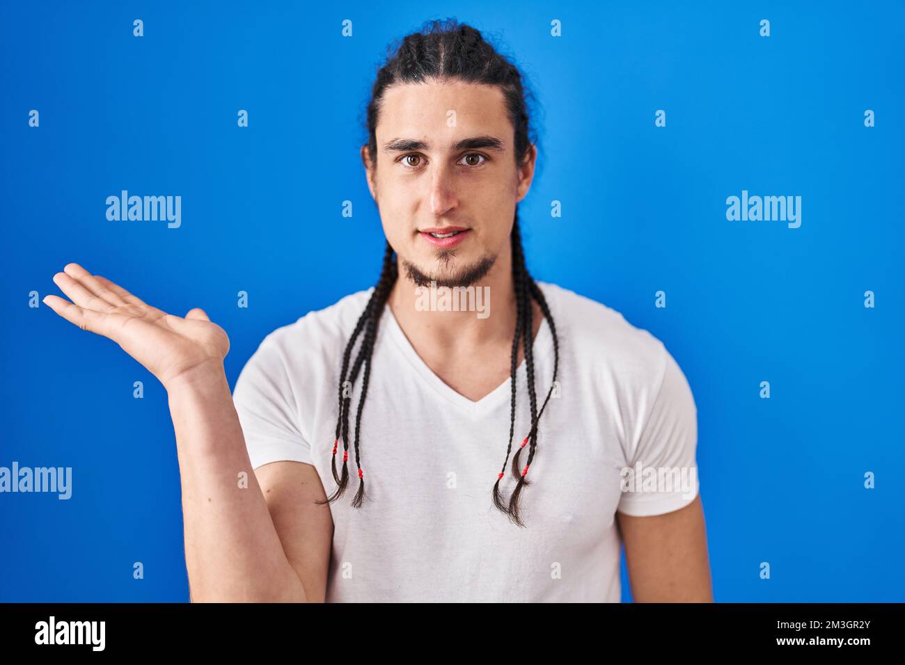 Hispanic man with long hair standing over blue background smiling ...