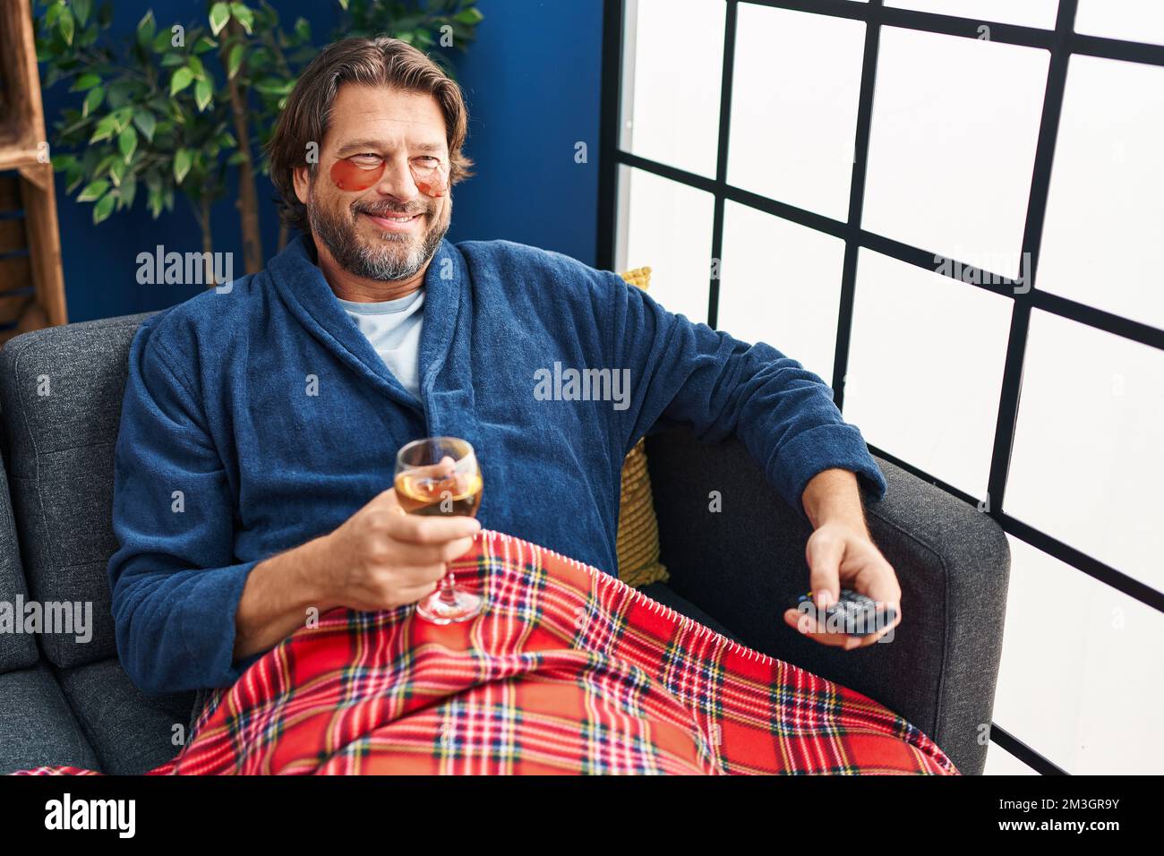 Middle age man wearing under eye patches watching television at home ...