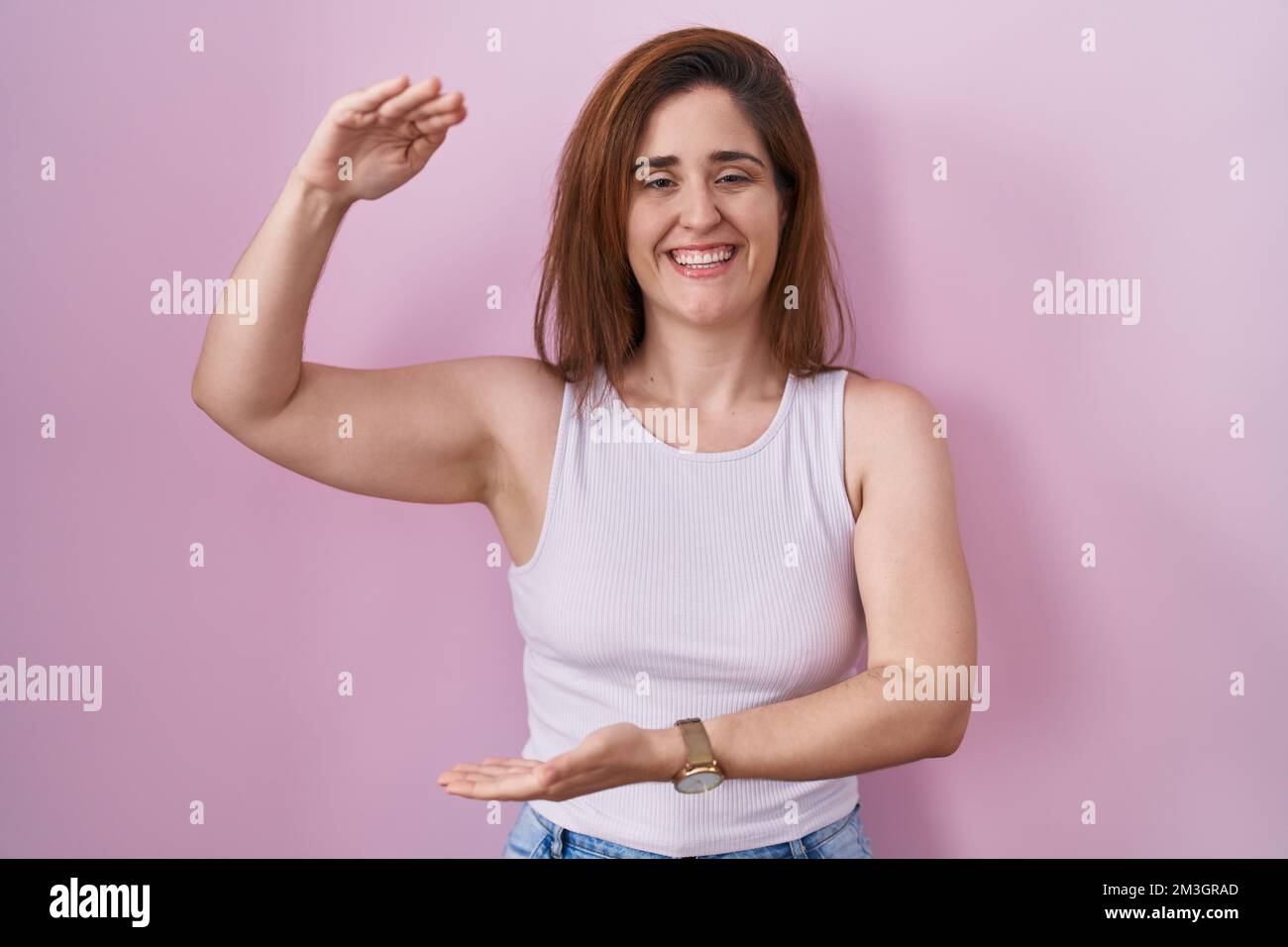 Brunette woman standing over pink background gesturing with hands ...