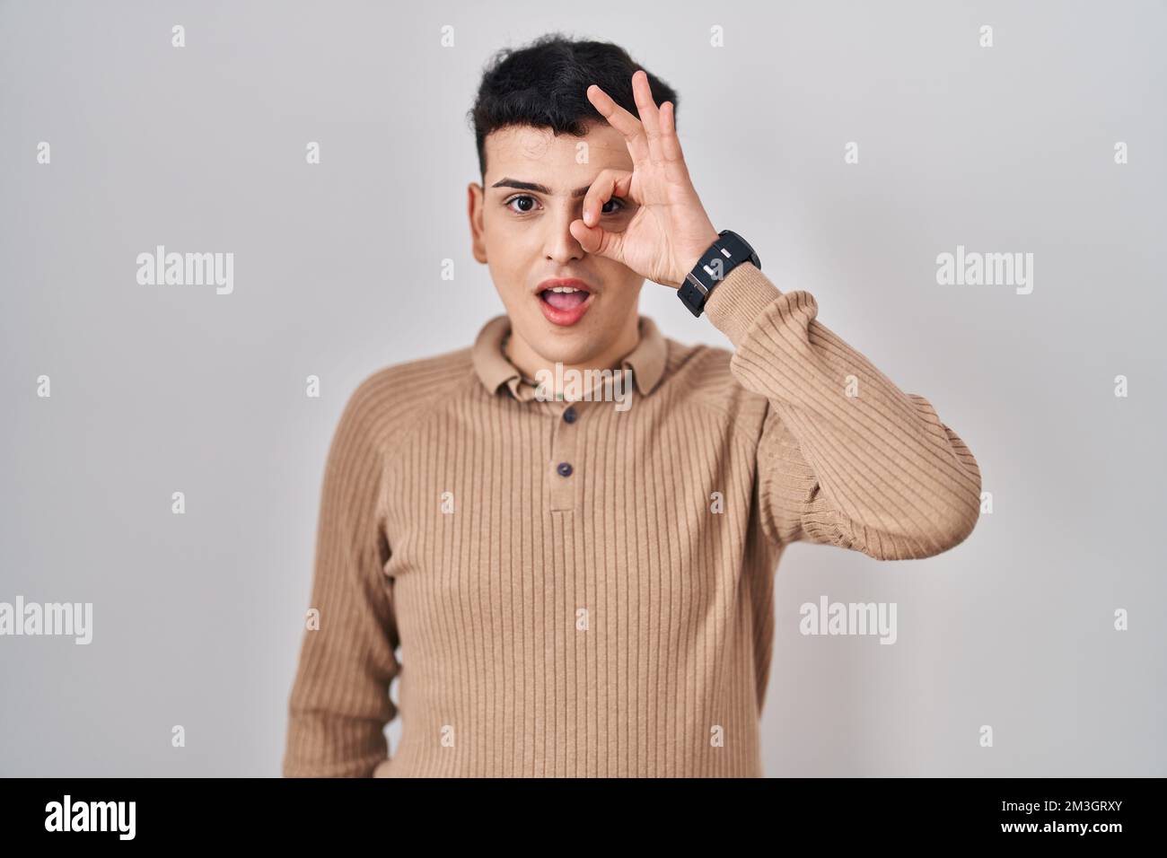 Non binary person standing over isolated background doing ok gesture ...