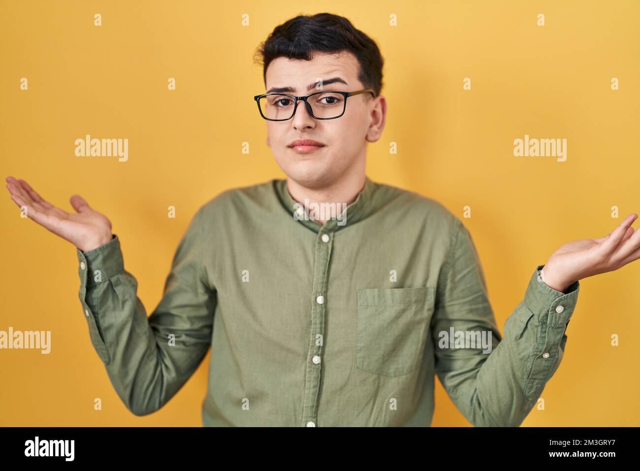 Non binary person standing over yellow background clueless and confused ...