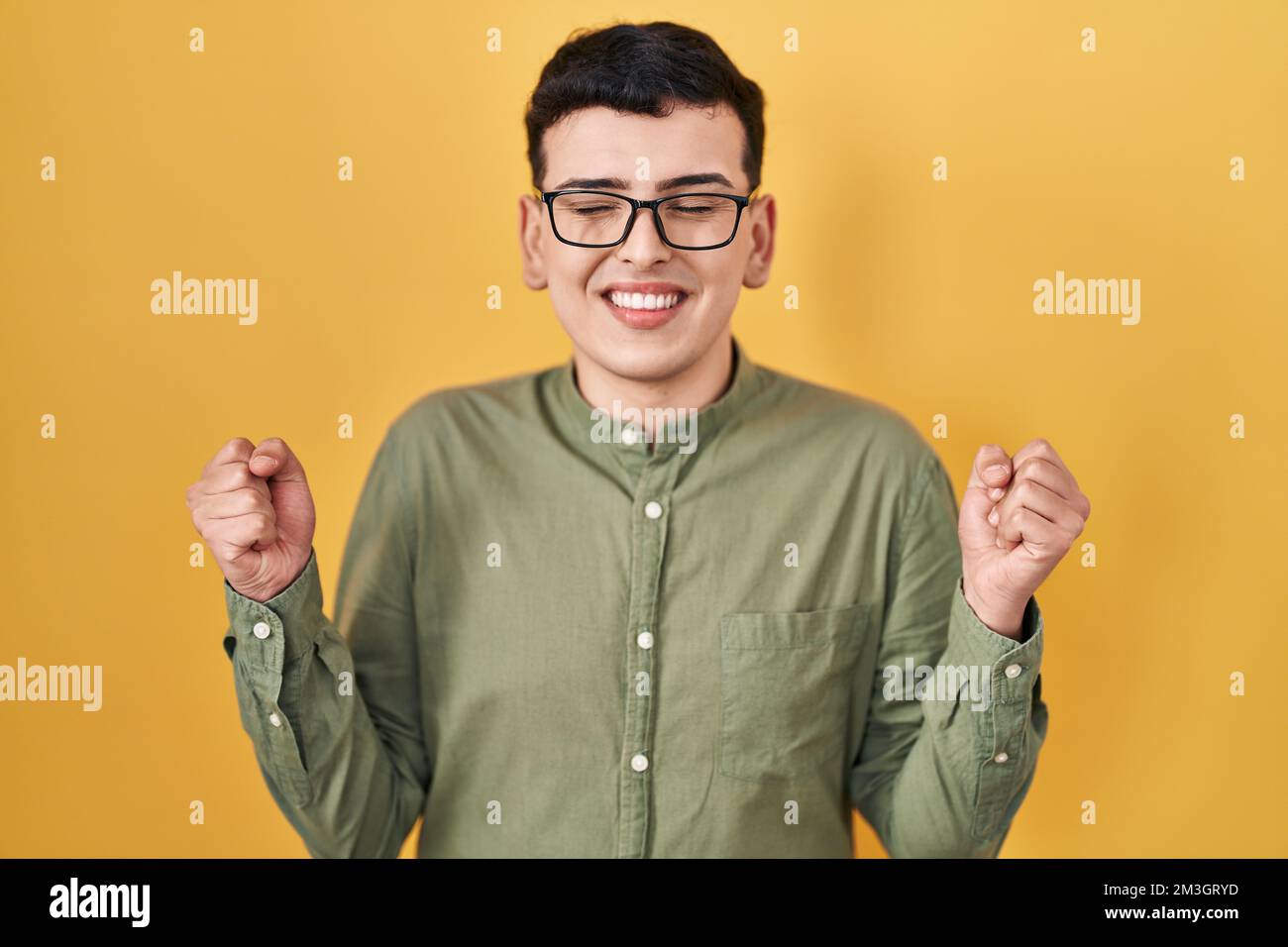 Non binary person standing over yellow background excited for success ...