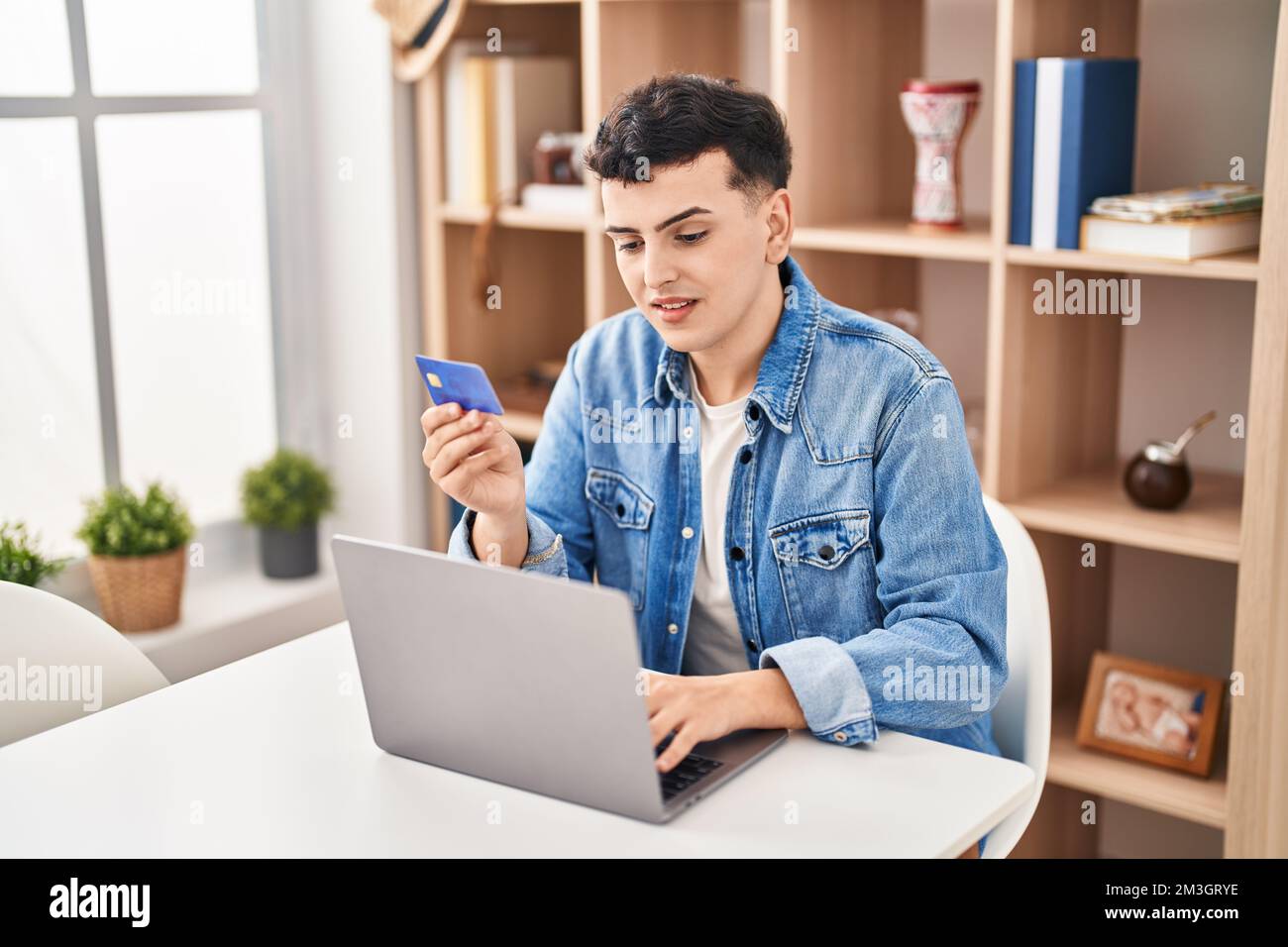 Young non binary man using laptop and credit card sitting on table at ...