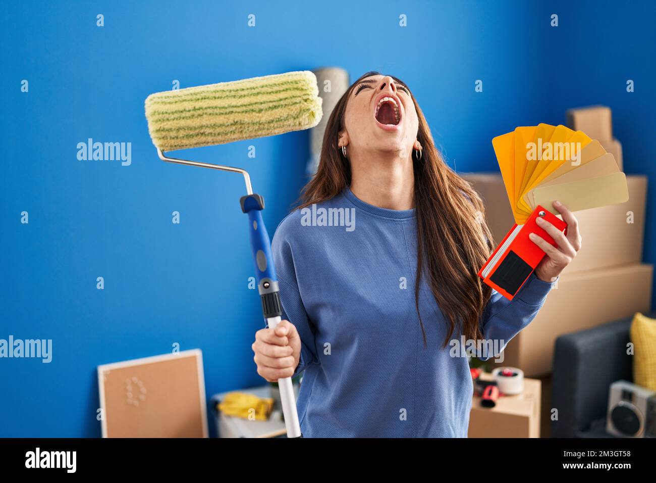 Young brunette woman holding roller painter painting new house angry ...