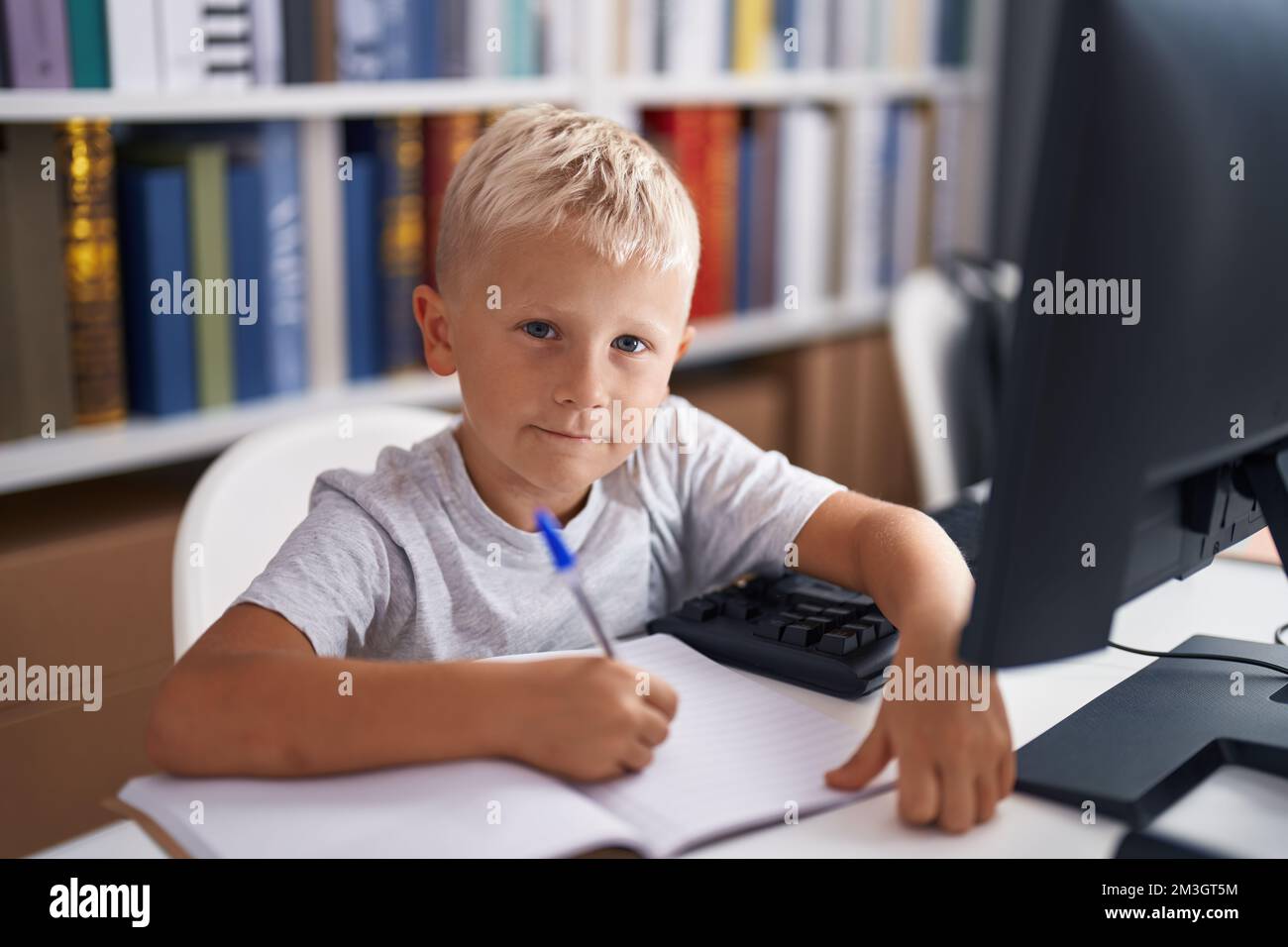 Adorable toddler student using computer writing on notebook at ...