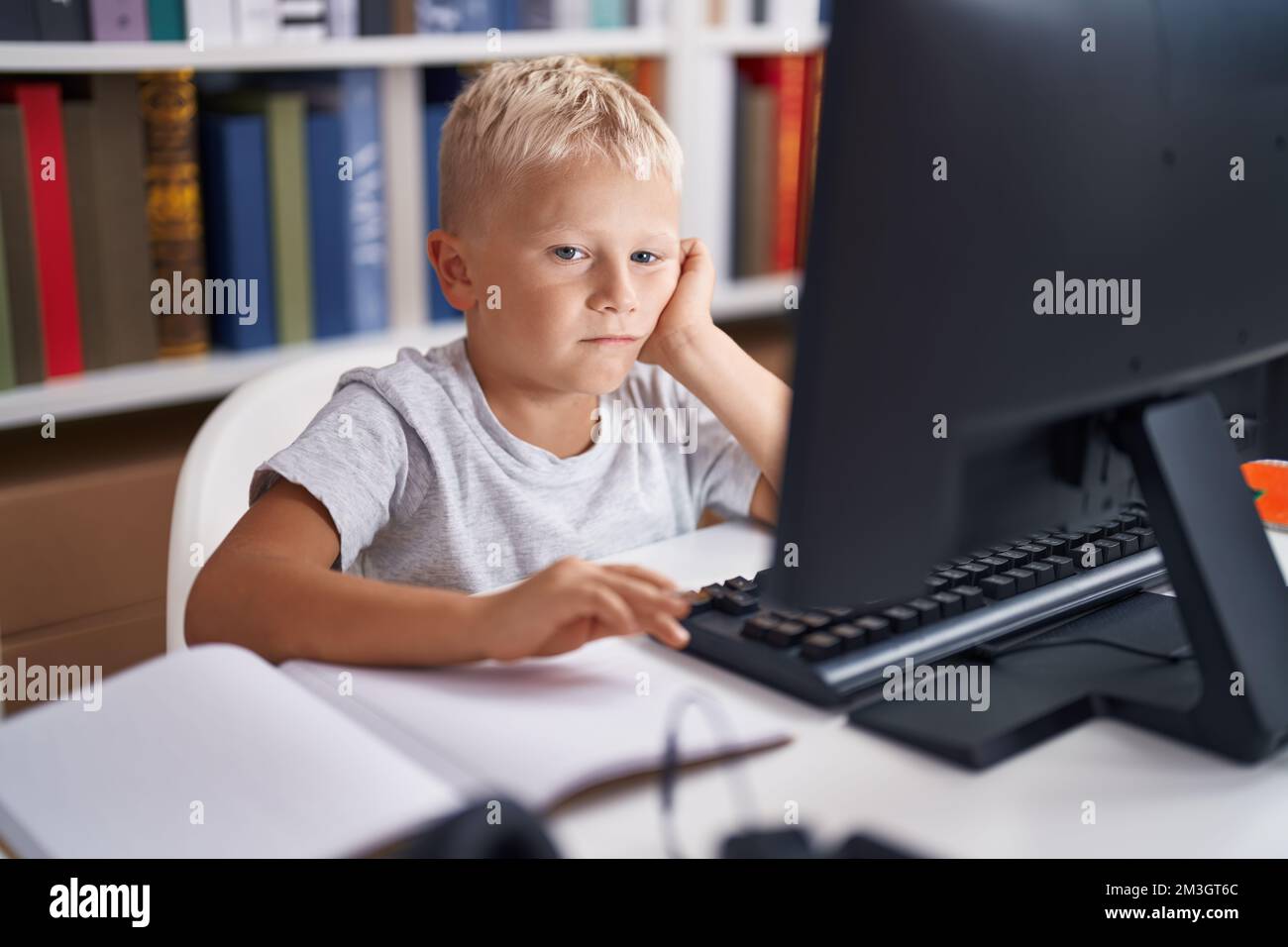Adorable toddler student boring using computer sitting on table at ...