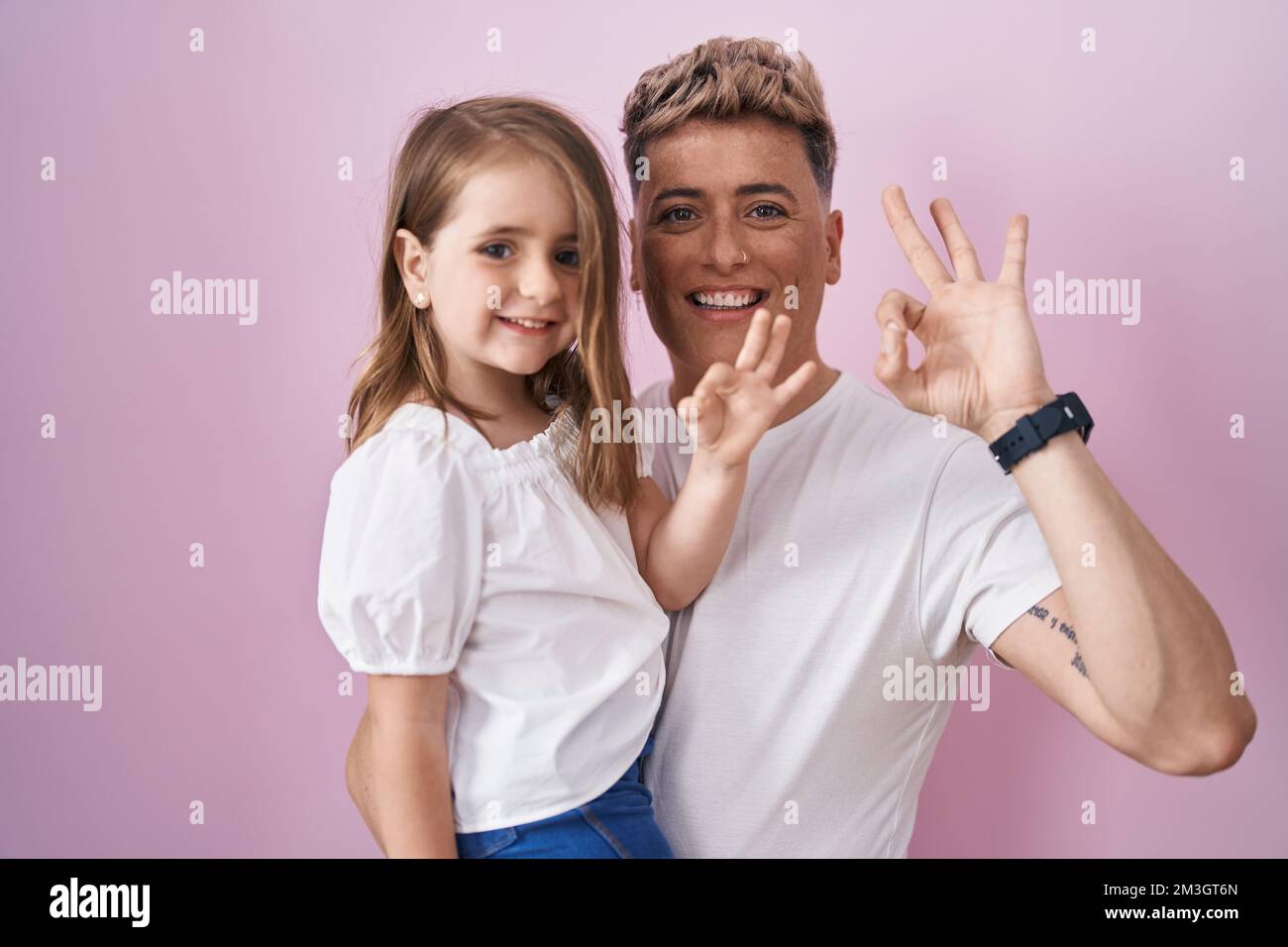 Young father hugging daughter over pink background doing ok sign with ...