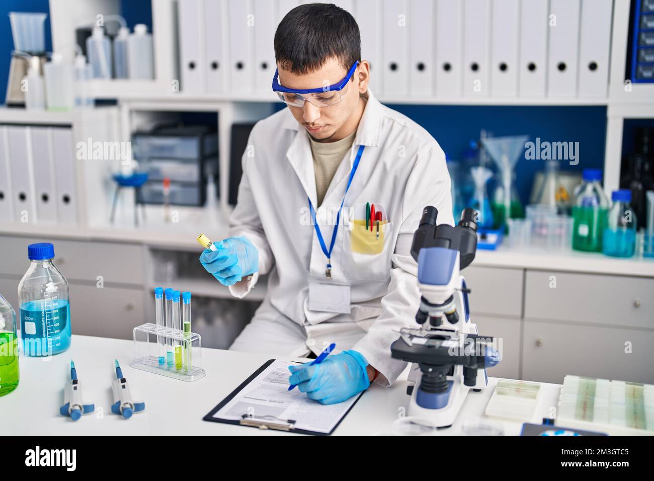Young man scientist writing on document measuring liquid at laboratory ...