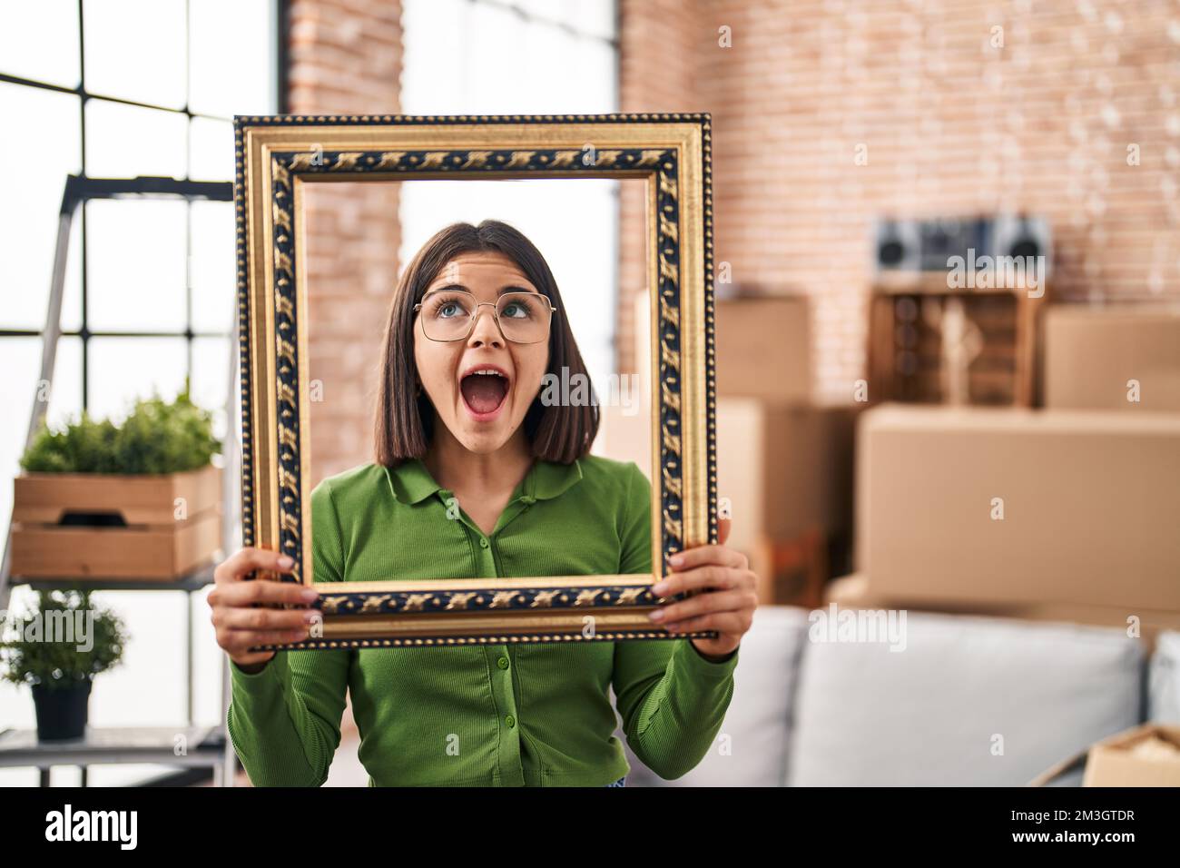 Young hispanic woman at new home holding empty frame angry and mad ...