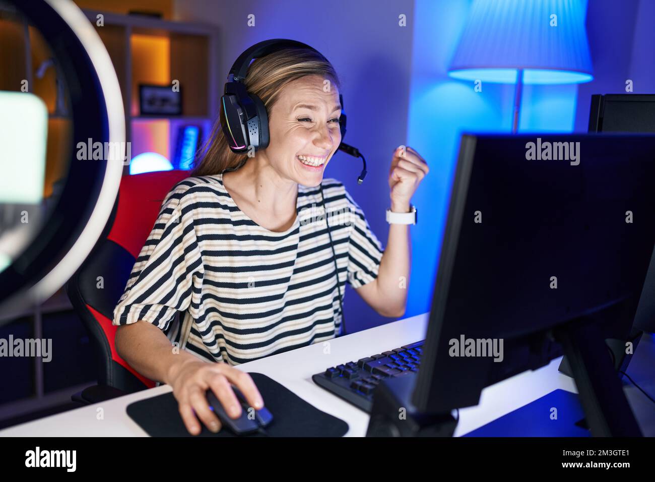 Young blonde woman streamer playing video game with winner expression ...